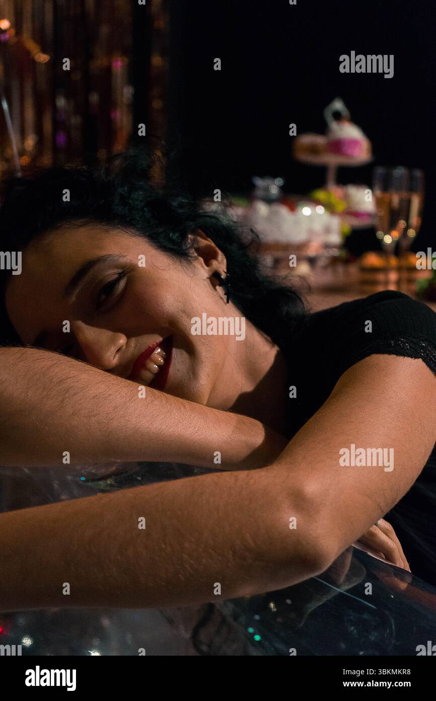 The image depicts a woman in a relaxed pose on a table, smiling warmly ...