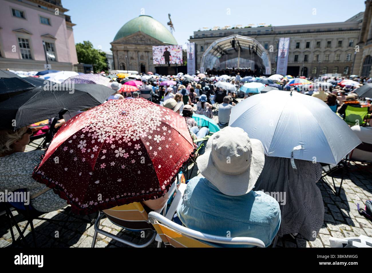 22 June 2025, Berlin: People with umbrellas watch the Staatskapelle ...