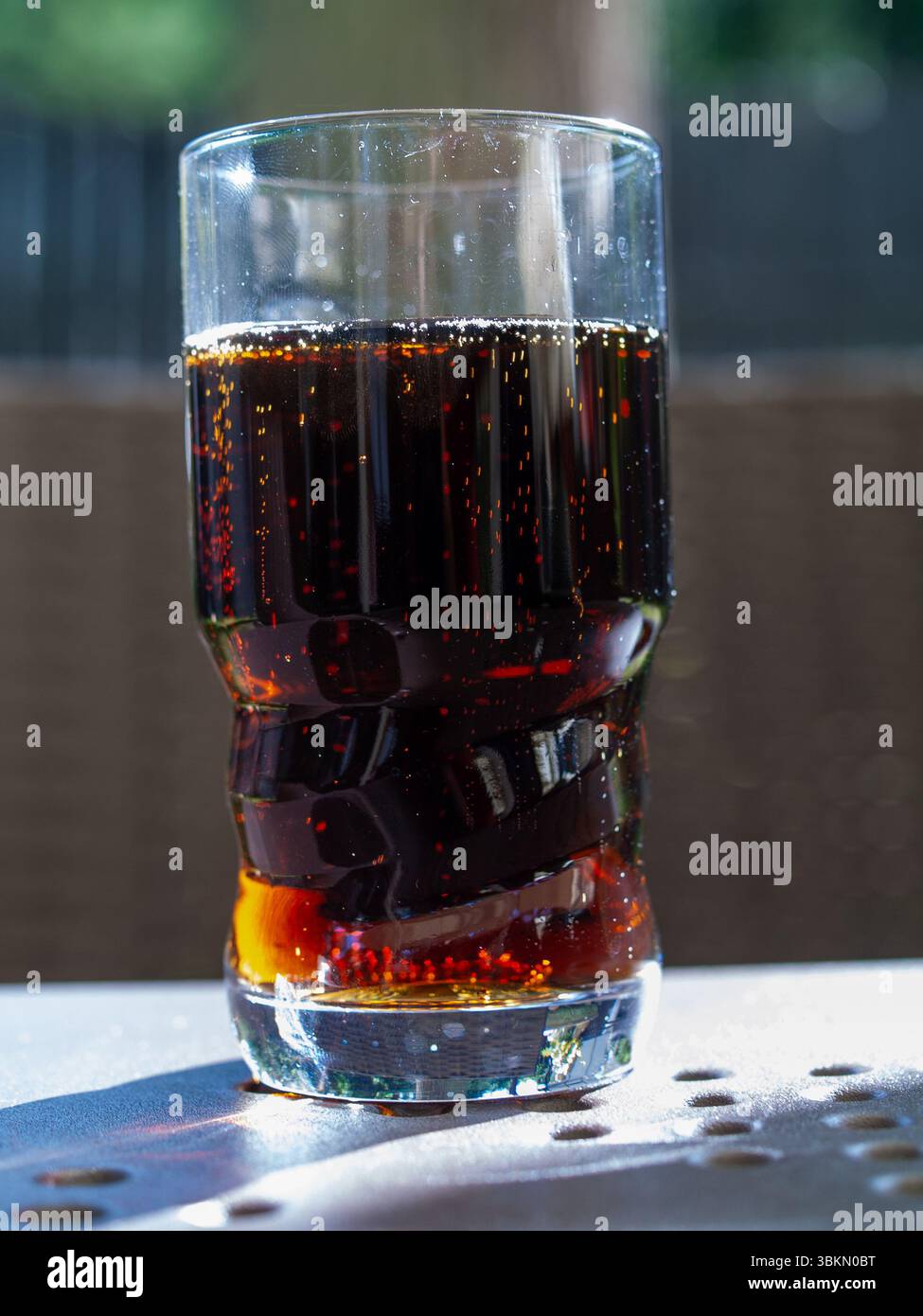 Glass of dark soda sits on a table. The glass is half full and the soda ...