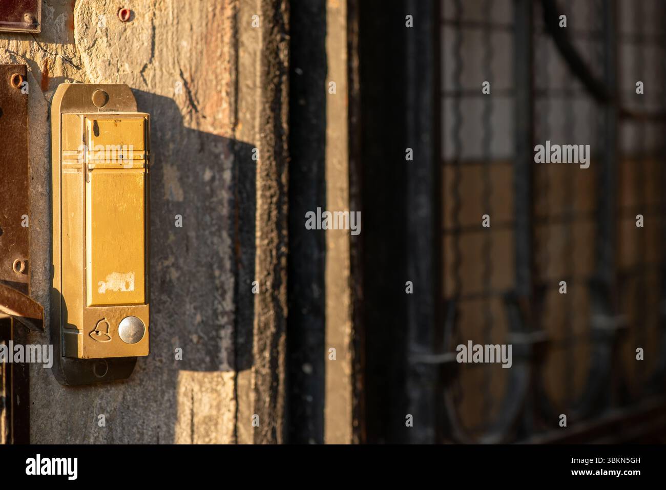 A retro golden intercom on a rough stone wall with a blurred gate ...