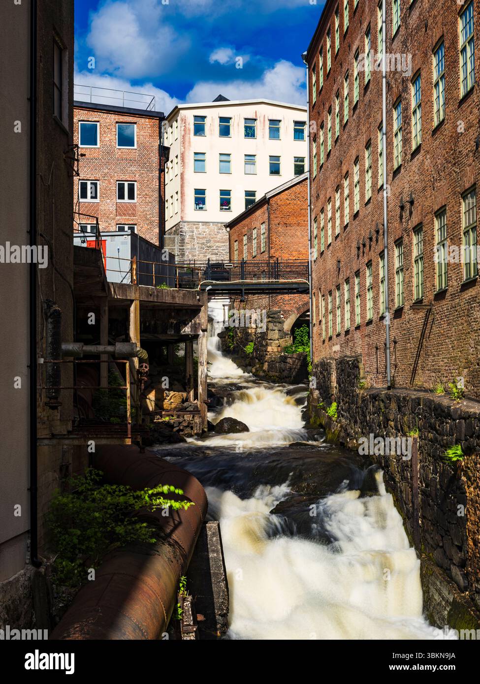 A waterfall cascades through the narrow passage between old industrial ...