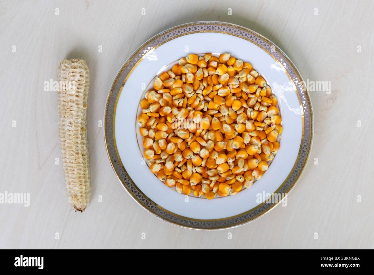Corn seeds separated from cob in ceramic plate on wood. Overhead shot ...