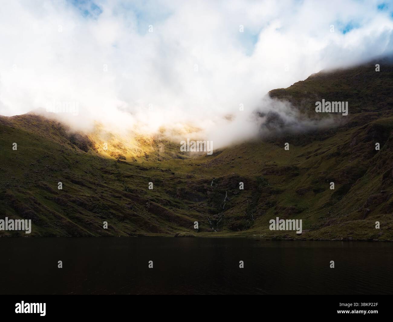 A still body of water is nestled between rolling, grass covered hills ...