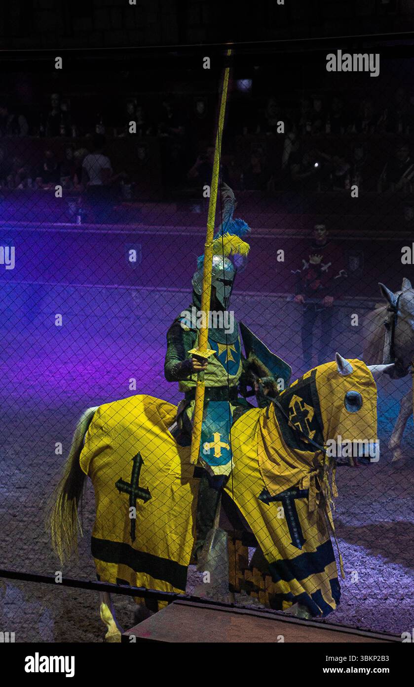 A knight dressed in armor rides a horse in a jousting arena, holding a ...
