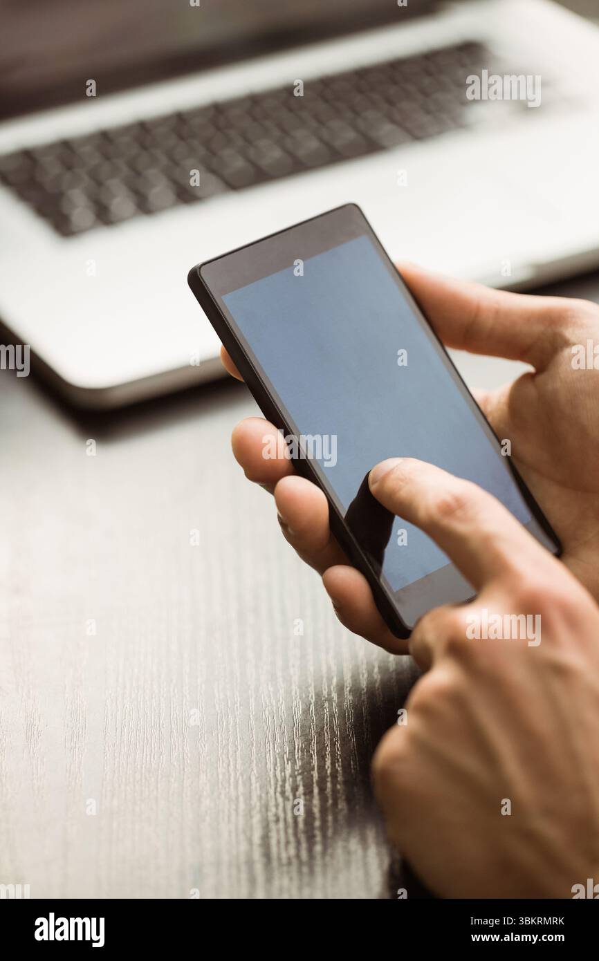 Hands are holding black smartphone and tapping screen above laptop on ...