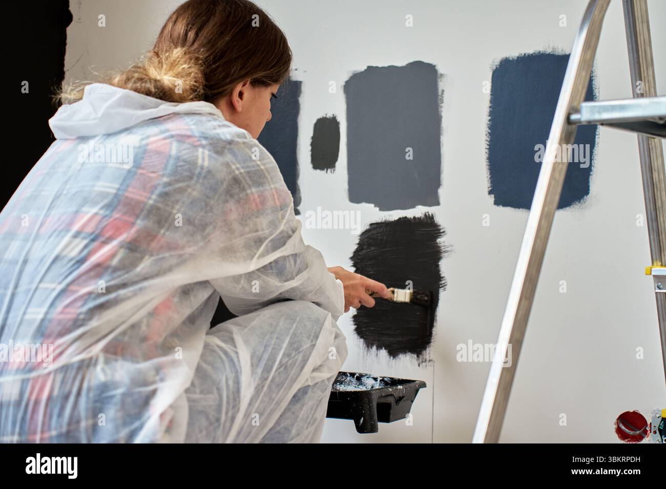 Woman in protective wear applies different dark paint swatches on white ...