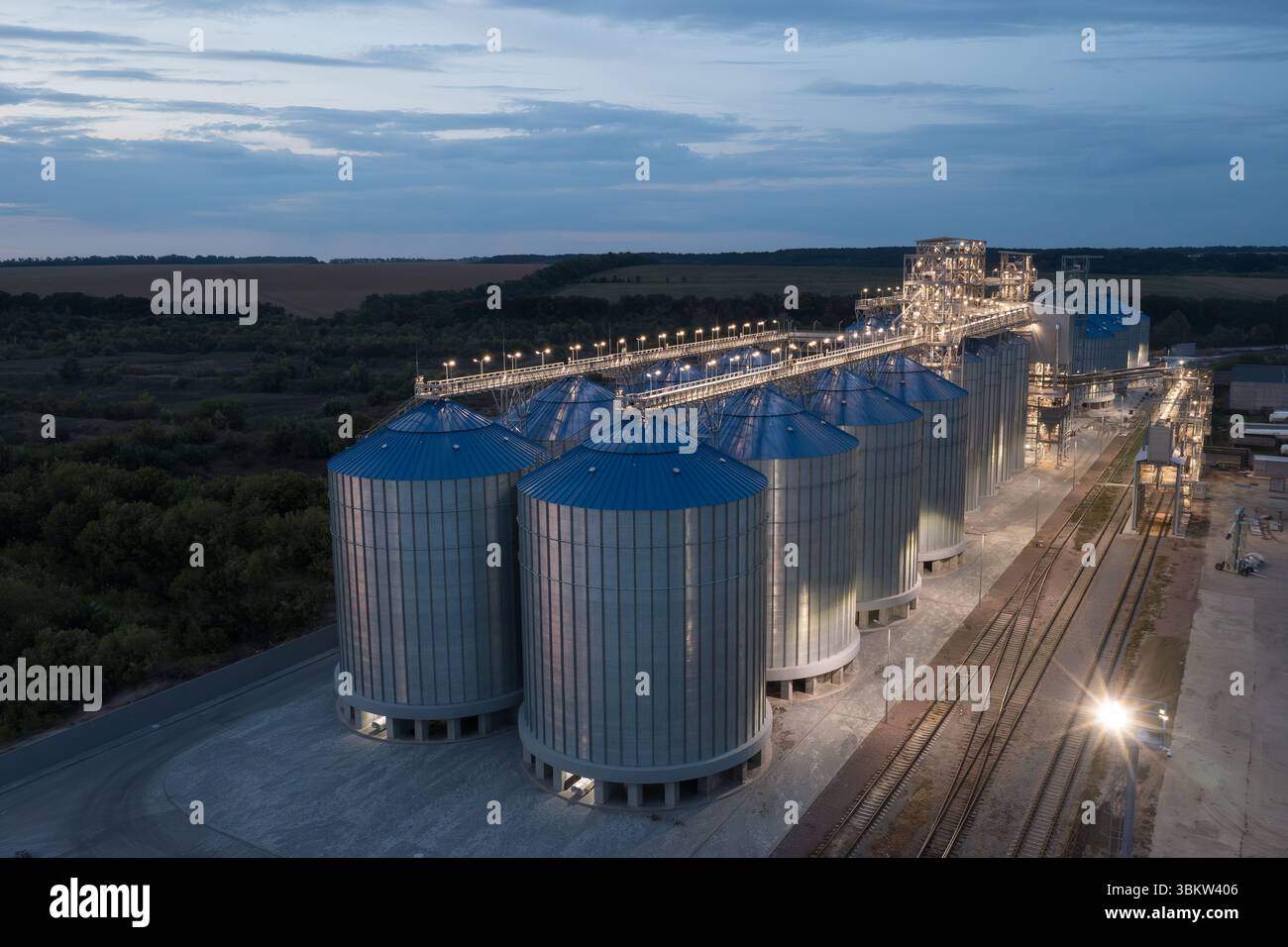Aerial night view of large illuminated grain silos and modern elevator facility with railway for ...