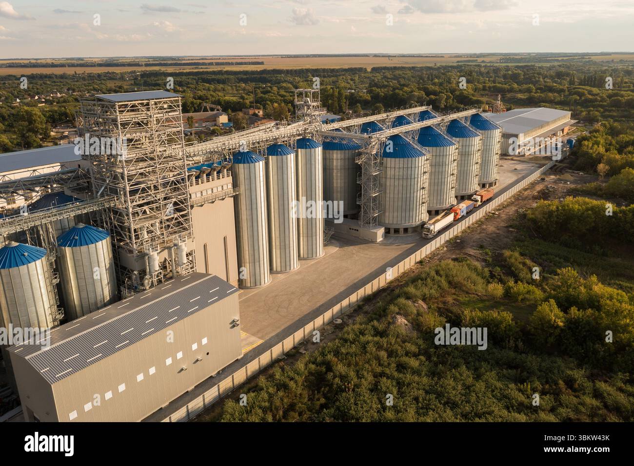 Aerial drone view of modern grain elevator complex with storage silos, trucks, and fields ...
