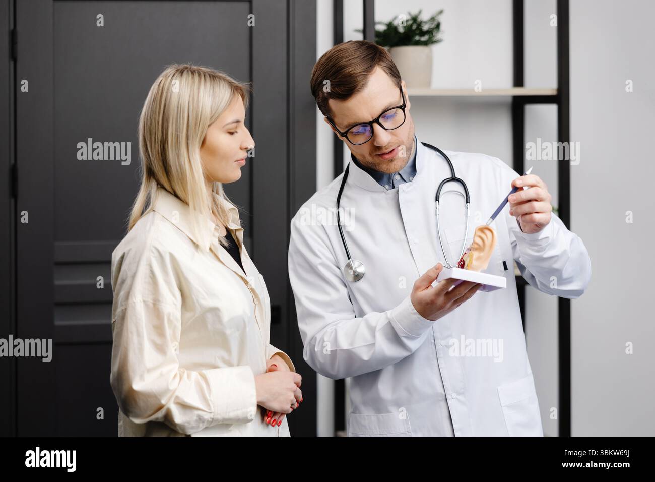 A young attractive otolaryngologist doctor shows a model of the ear and ...