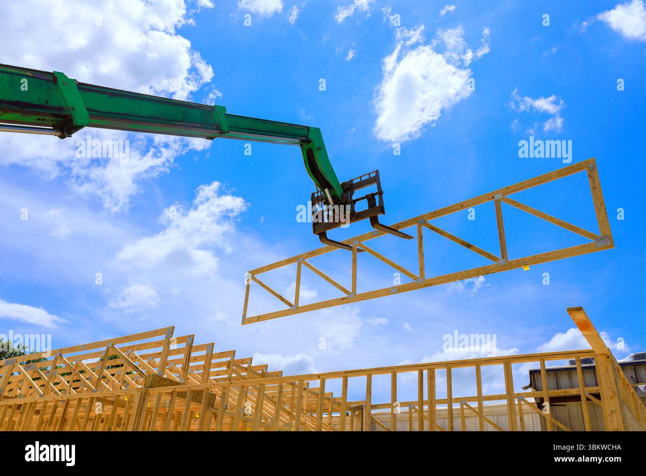 Forklift telehandler crane lifts large wooden truss into place, helping ...