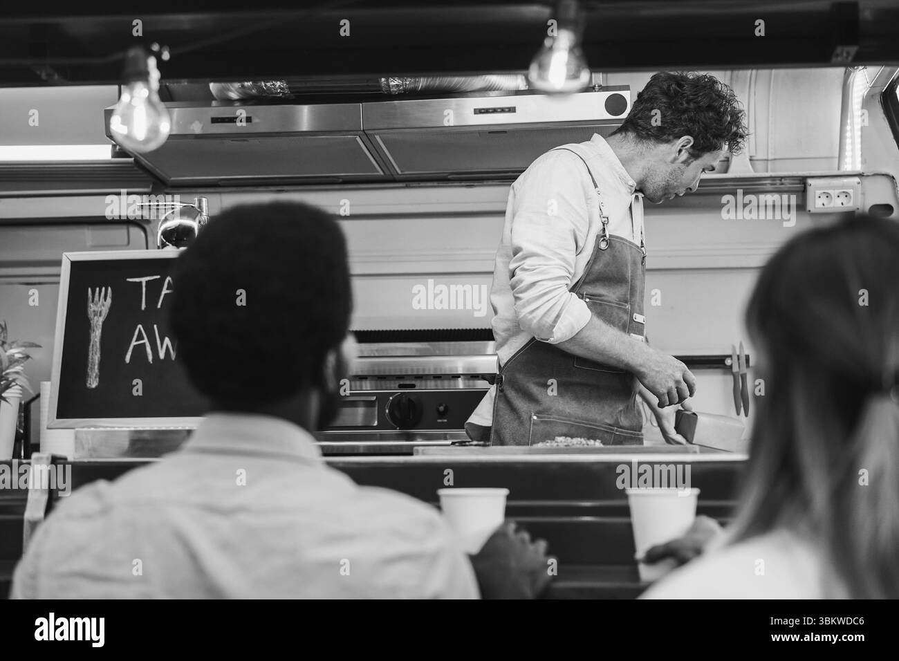 People are waiting outside of food truck while young chef preparing ...