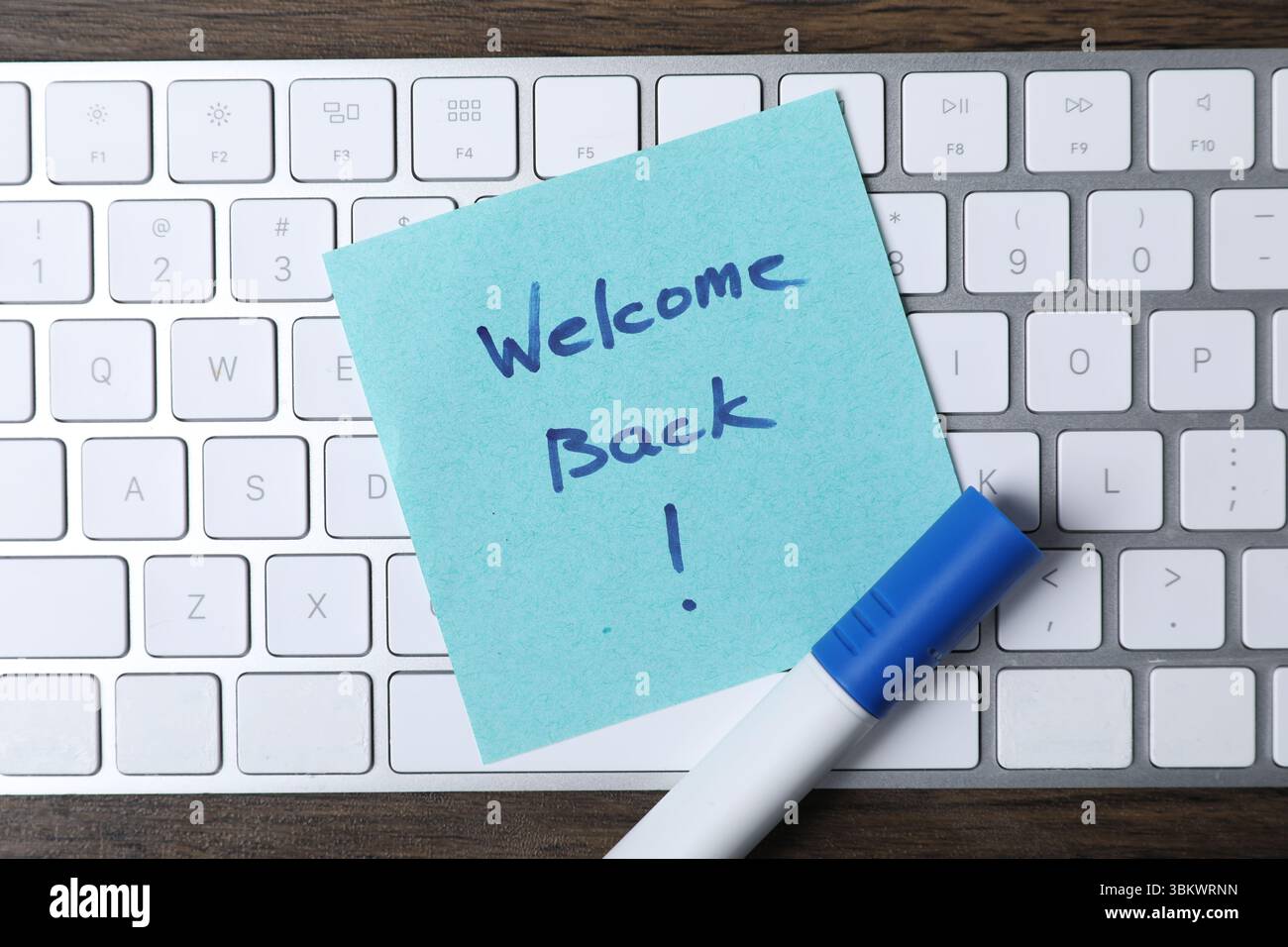 Paper note with phrase Welcome Back, marker and keyboard on table, top ...
