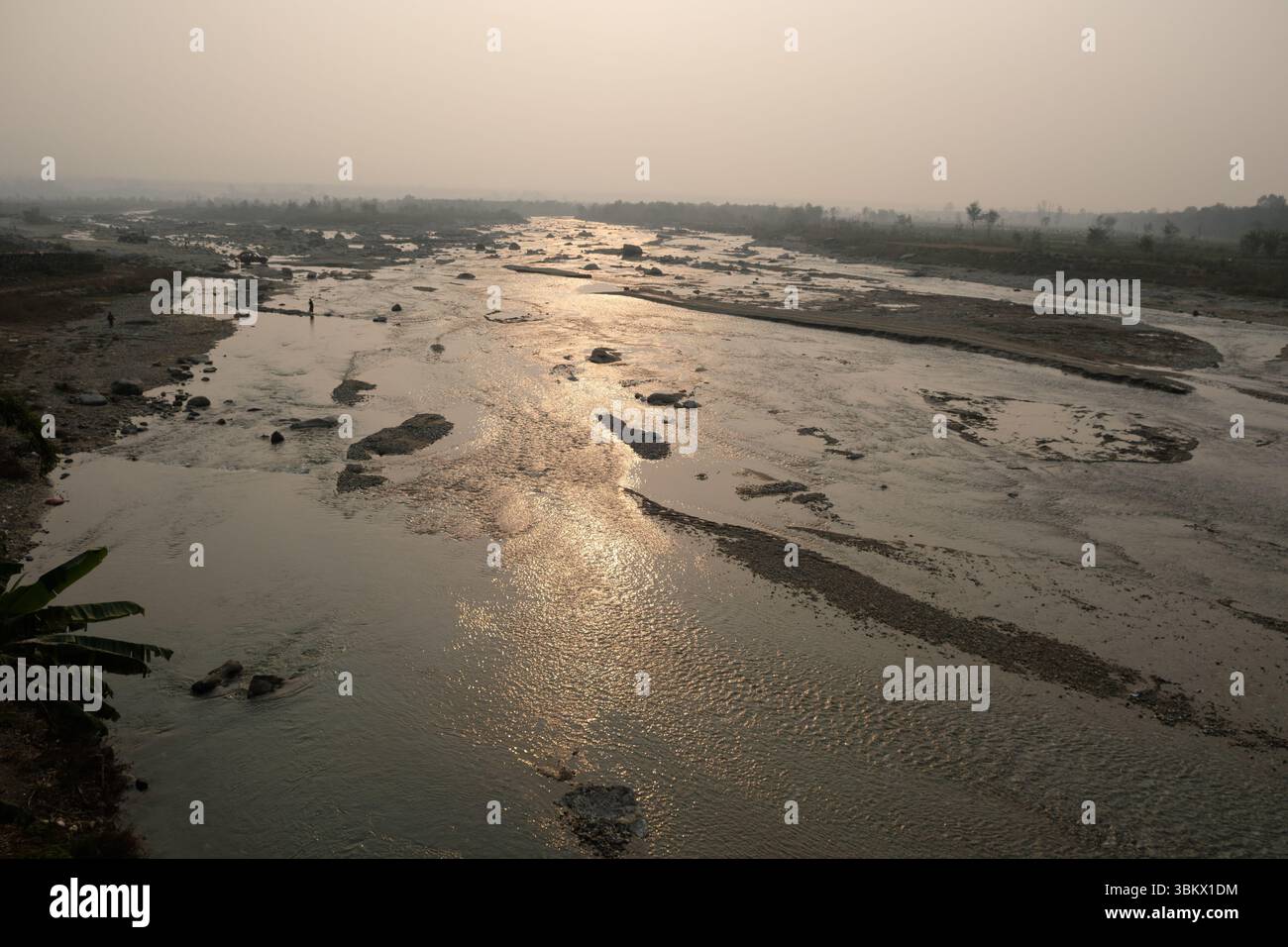 Sun reflects on wide riverbed with people & vehicles, likely collecting ...