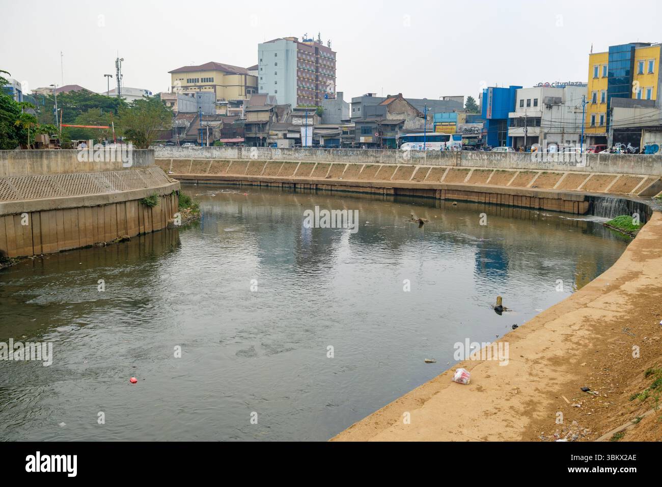 City buildings overlook a polluted urban river with concrete banks ...