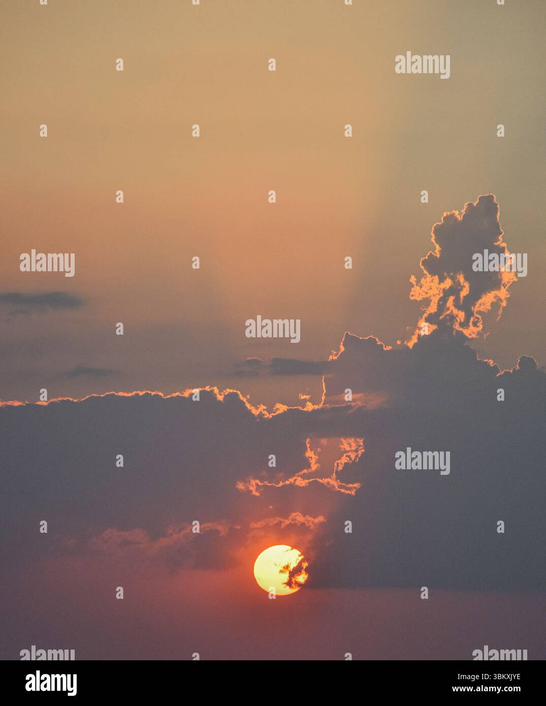 Radiant golden sun sets behind fiery clouds, sky shifting from orange ...