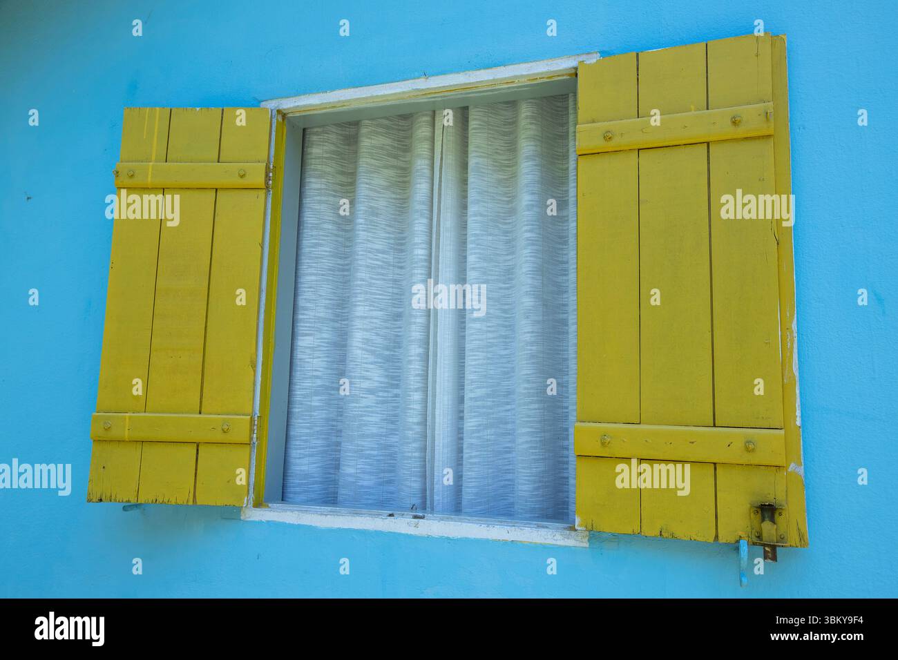 Decorative yellow window with white curtain on blue wall. Contryside of ...