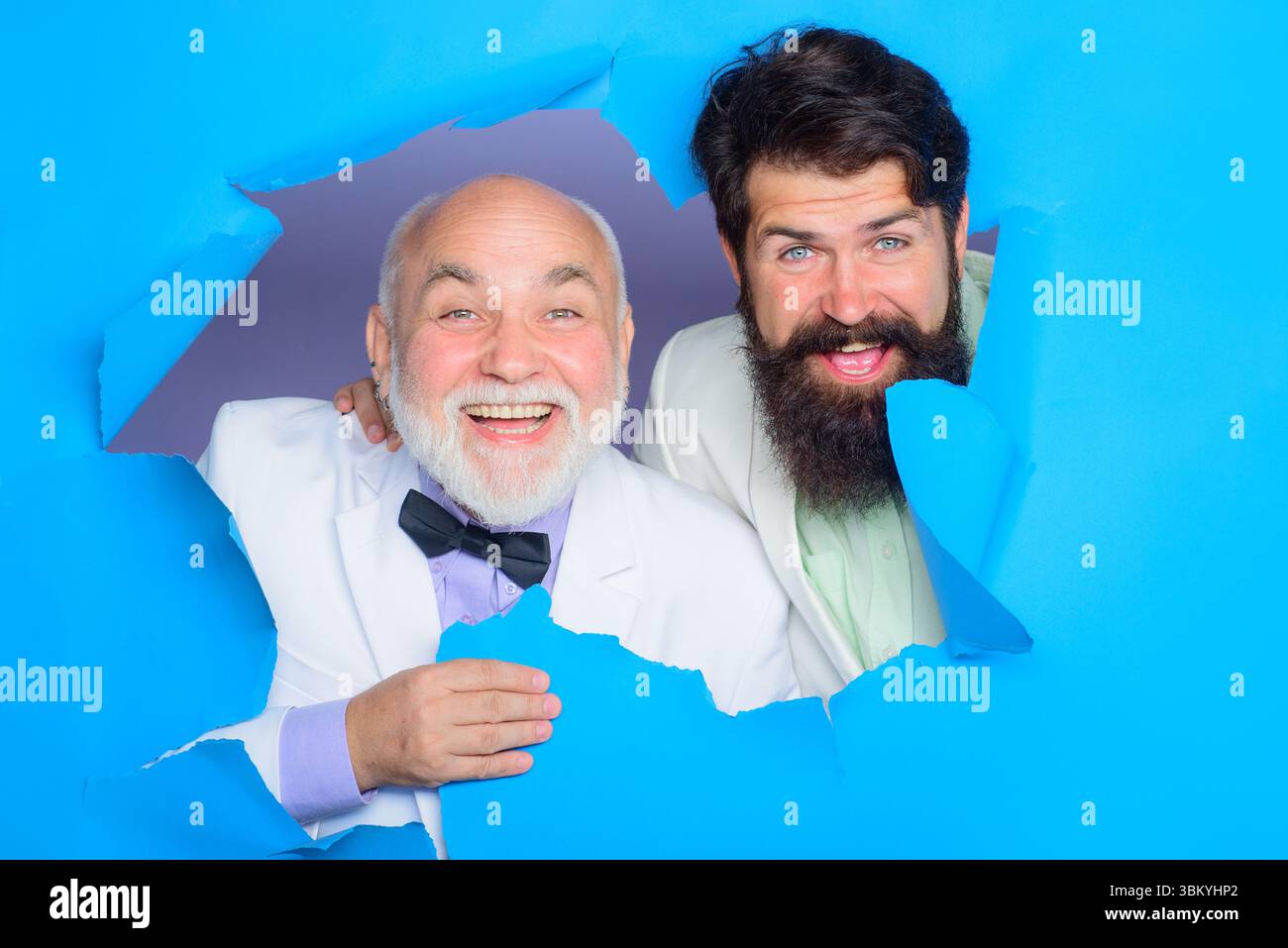 Successful bearded men looking through hole in paper. Happy adult son ...