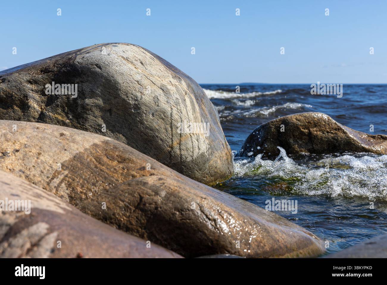Large rocks resting on the coastline as gentle waves rush by, with ...