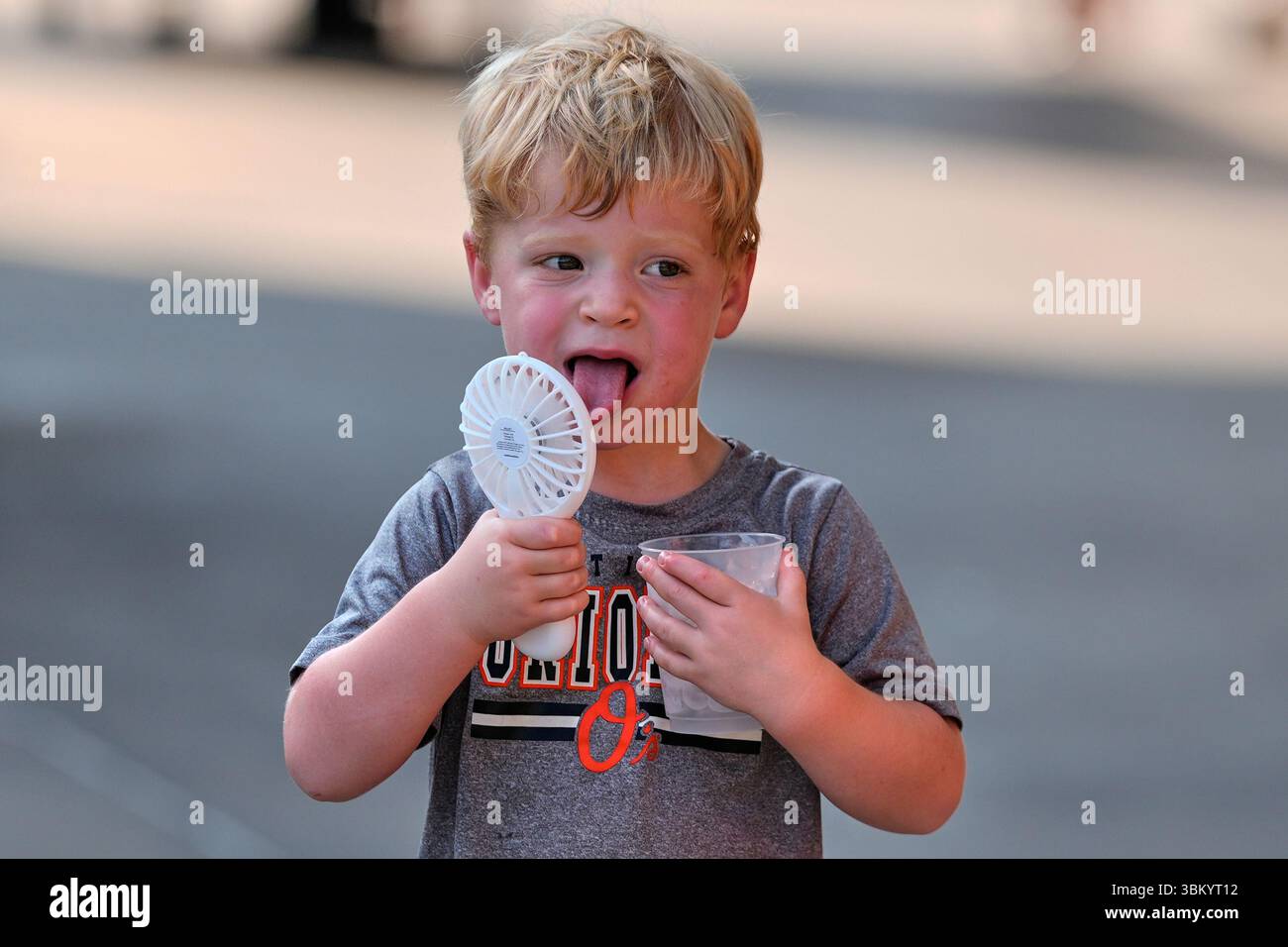 Asher Gillen, 3, uses a battery-powered fan while holding a cup of ice ...