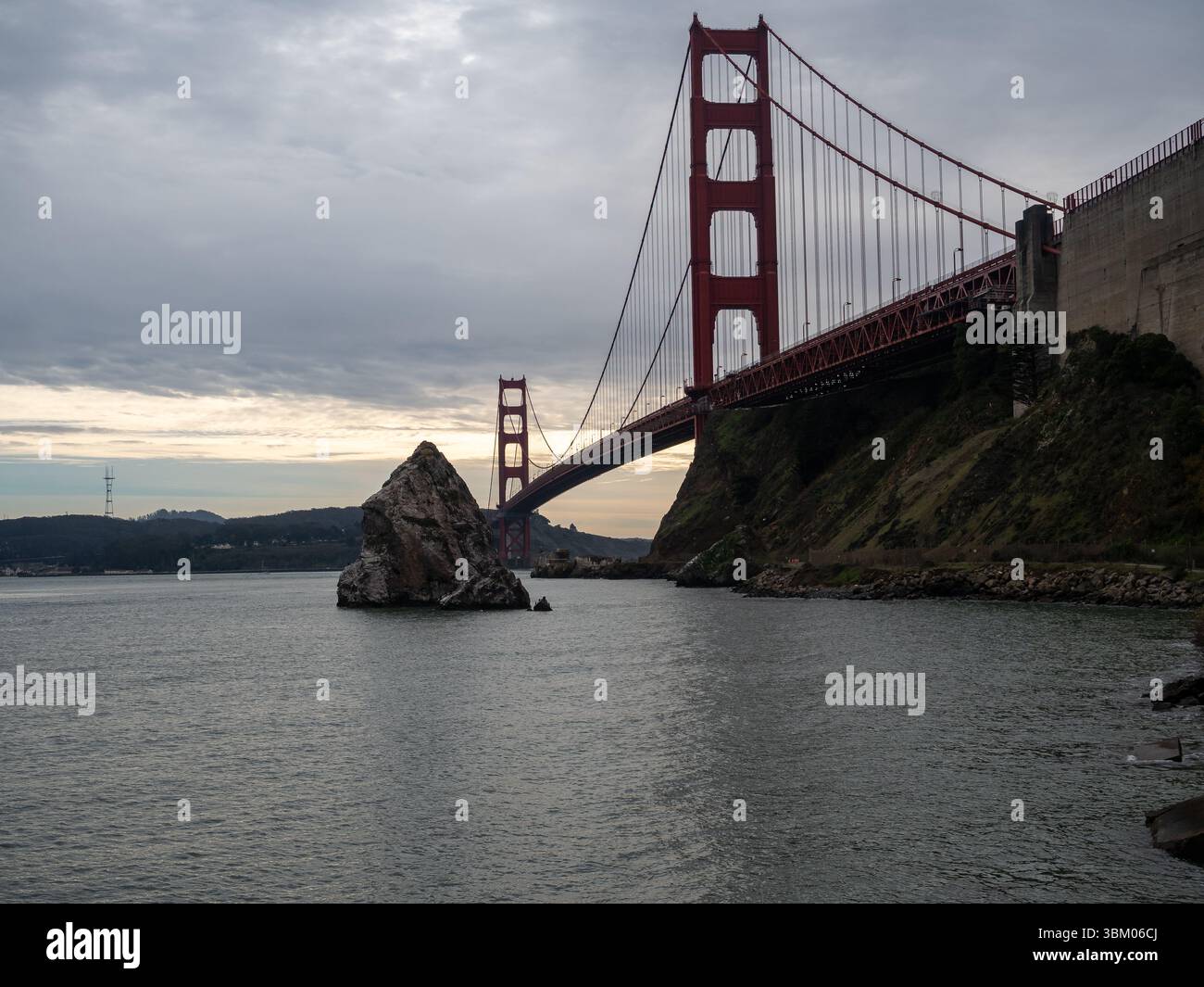 The Golden Gate Bridge is seen from the water, with a large rock ...