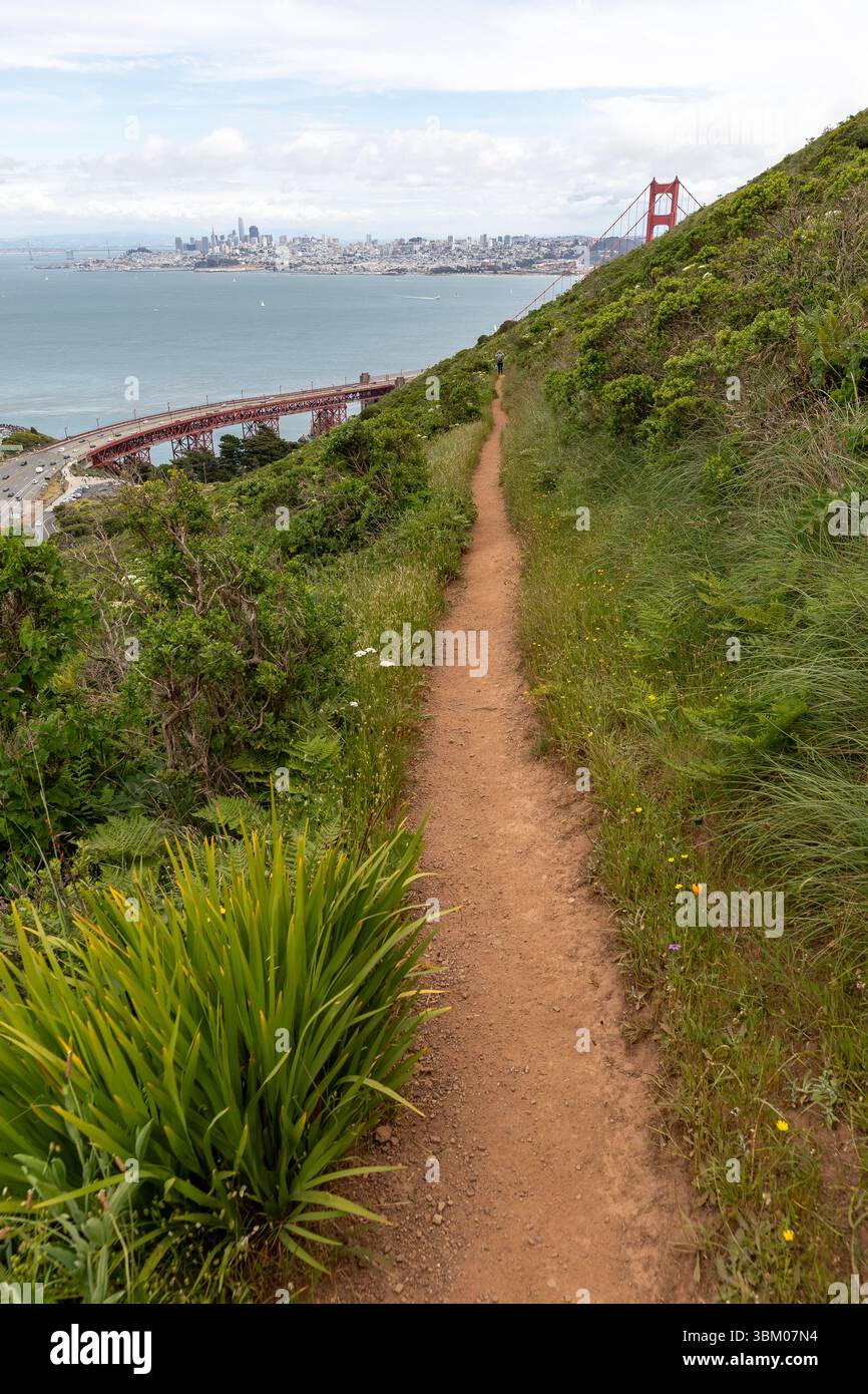 A person hikes along a dirt trail on a hillside overlooking the Golden ...
