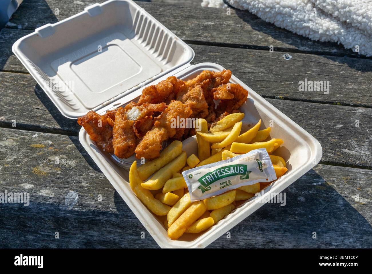 Fish and chips in a takeout container with fritessaus on a wooden ...
