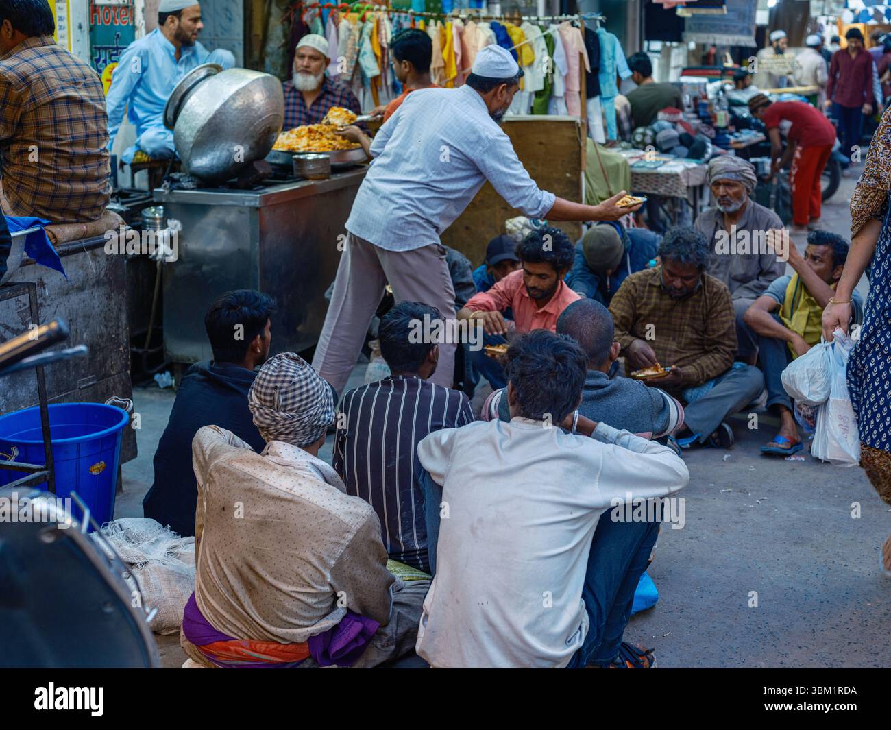 India, Kolkata, 16 Mar 2025. Men sit on a busy market street eating ...