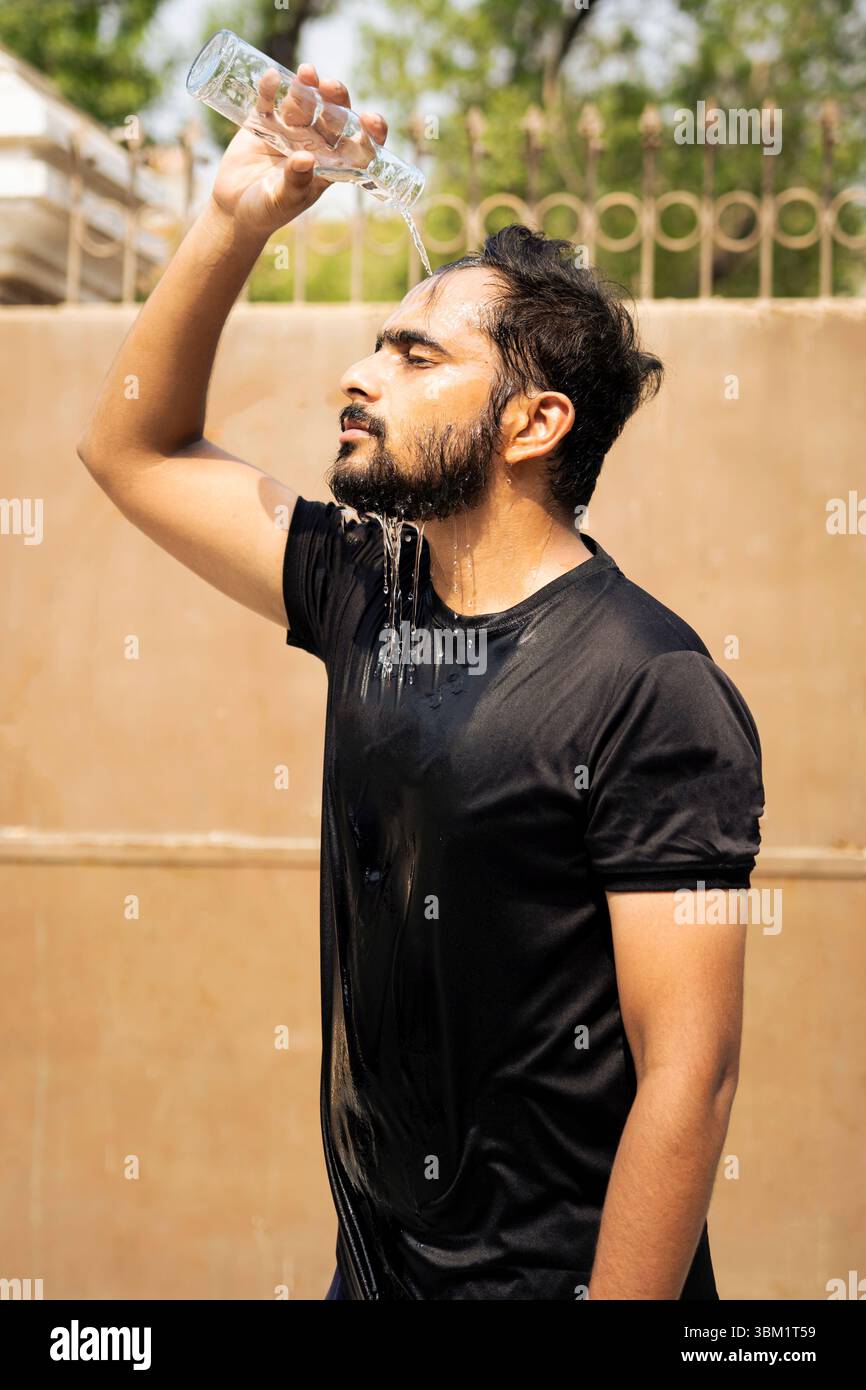 A young man with a beard is shown pouring water over his head from a ...