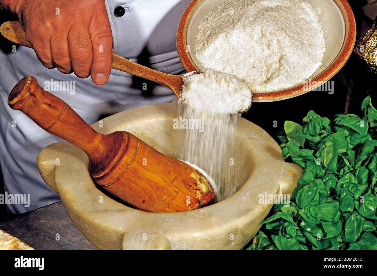 Chef is pouring grated cheese with wooden spoon into marble mortar with ...