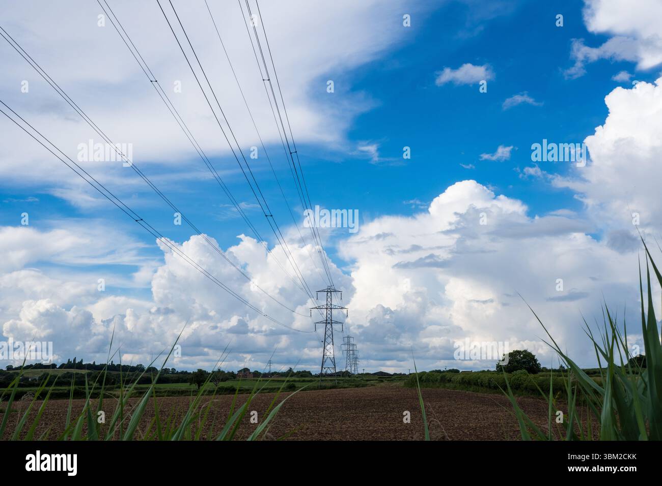 A line of electricity pylons in the countryside. With blue sky and ...