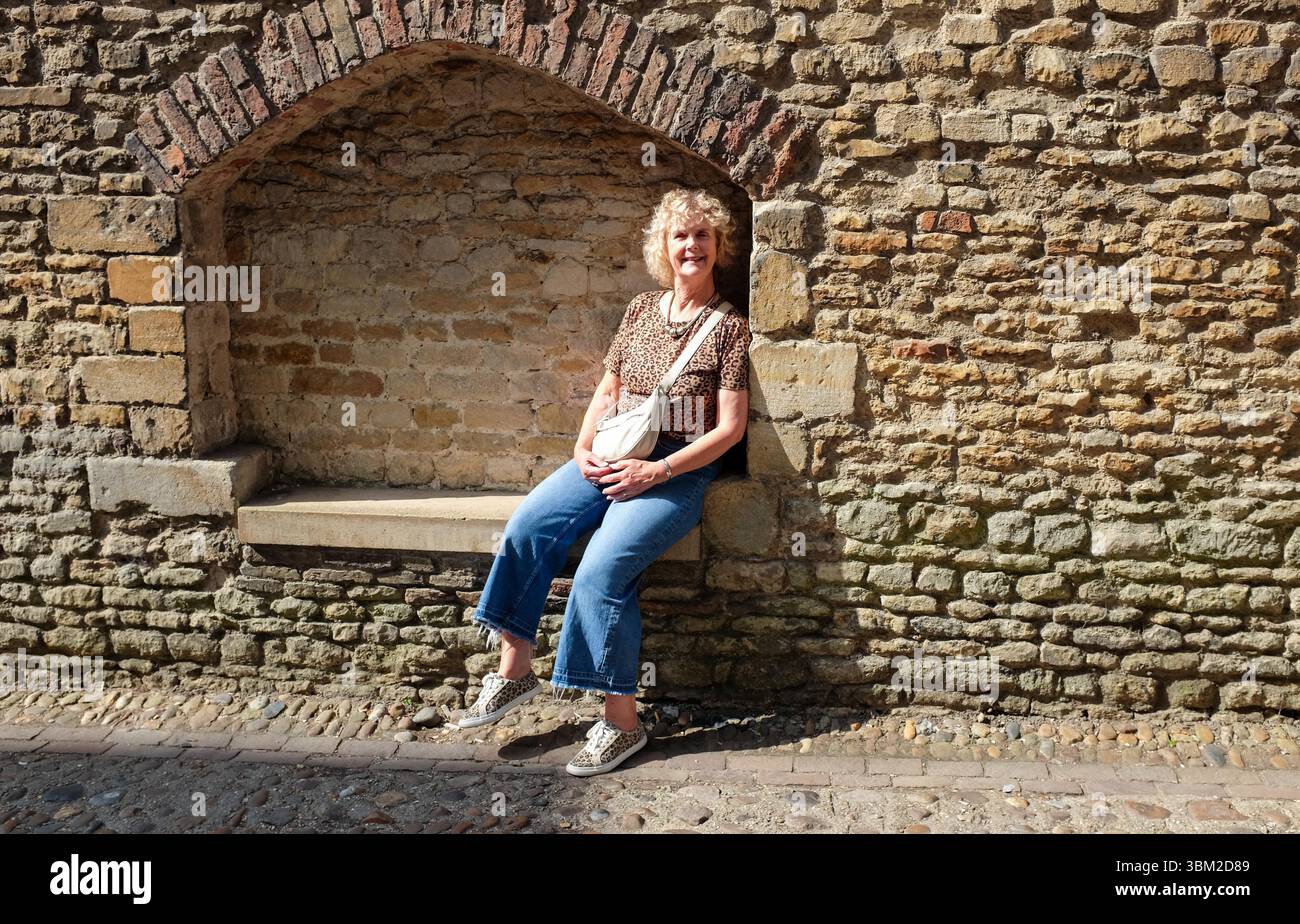 Cambridge UK June 2025 - Mature woman resting in wall seat in hot sunny ...