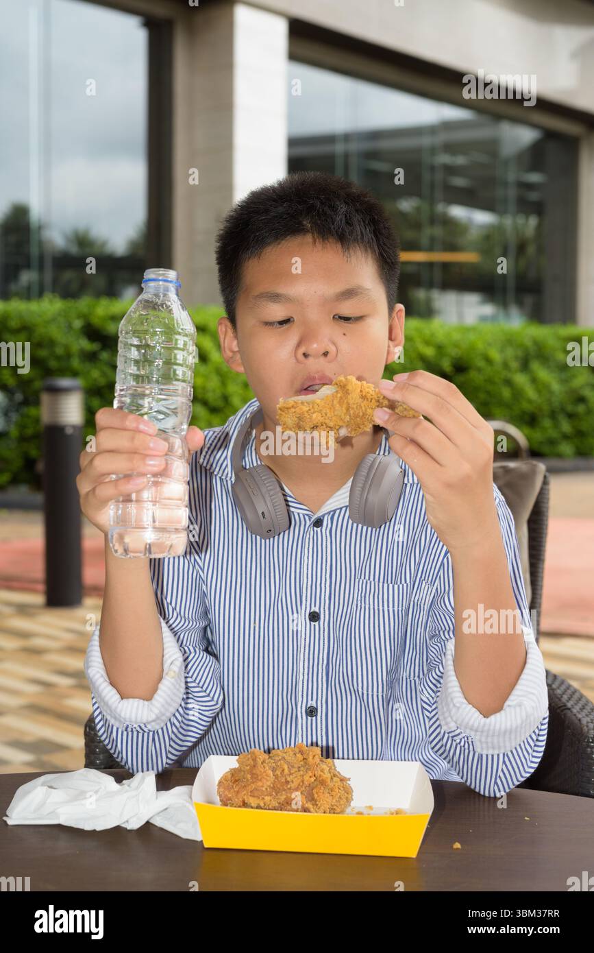 Thai student boy eating fried chicken and drinking water outdoors Stock ...