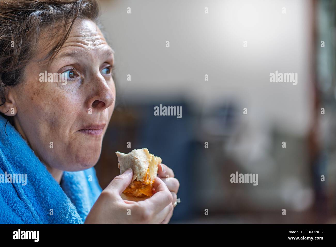 A woman is eating a sandwich and smiling. She is wearing a blue robe ...