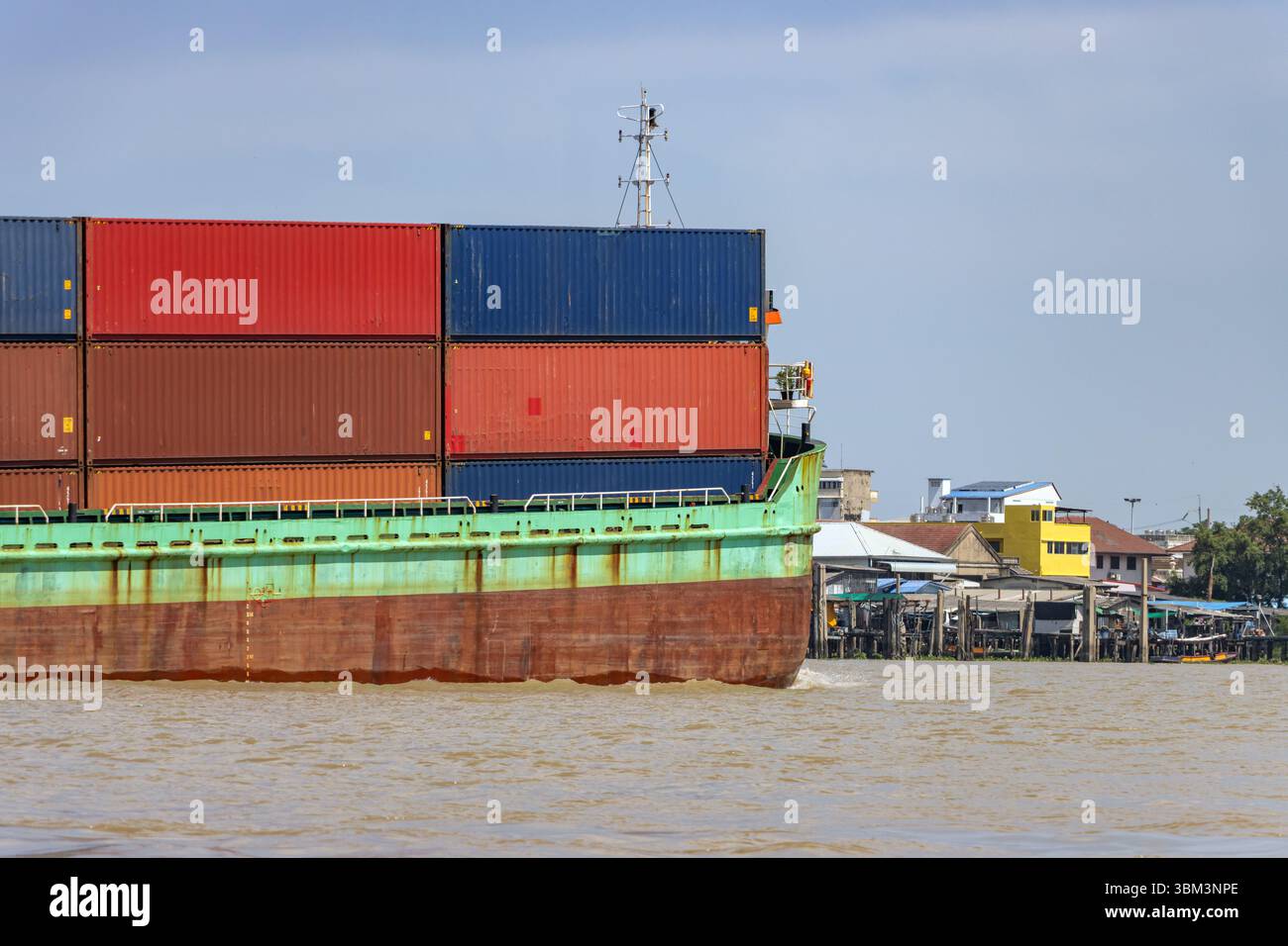 Cargo ship carrying stacked containers on a river near city waterfront ...