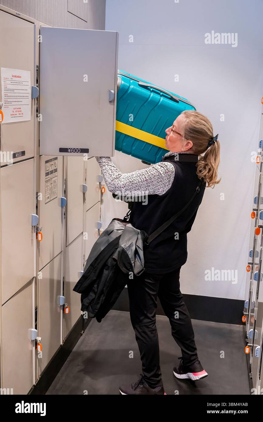 Japan, Takayama. Female tourist lifts a suitcase into a locker at the ...