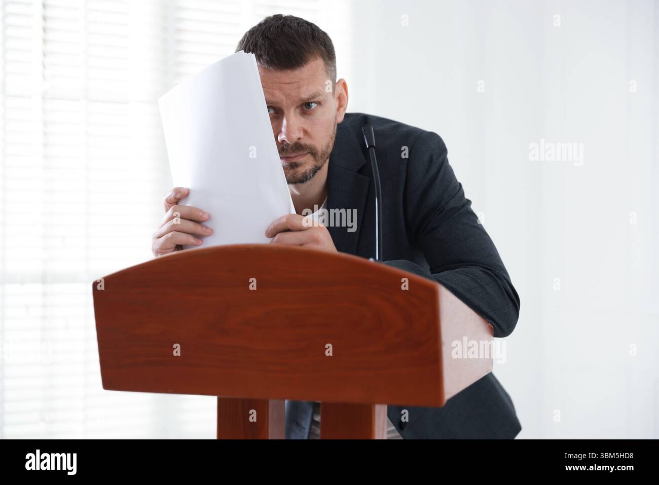 Fear of public speaking. Nervous man with microphone at lectern indoors ...