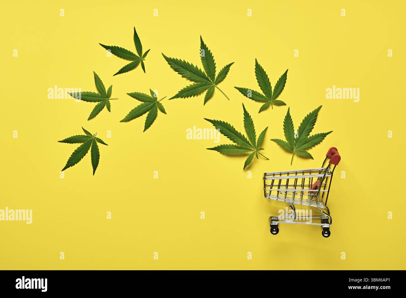 Shopping trolley and leaves of marijuana on yellow background. Legal ...