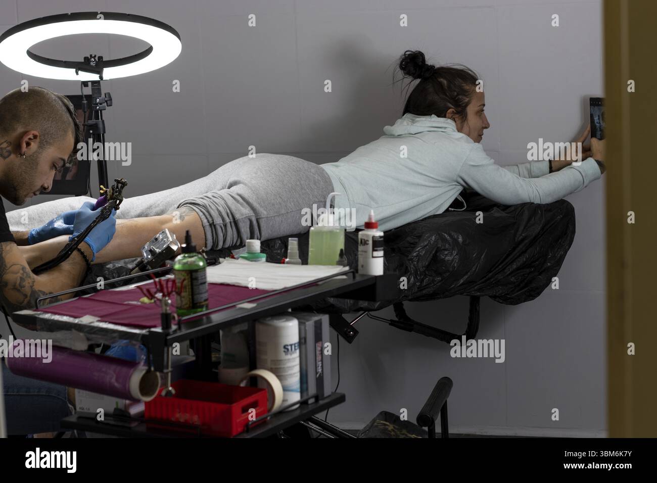 Young woman taking a selfie while having her leg tattooed by a ...