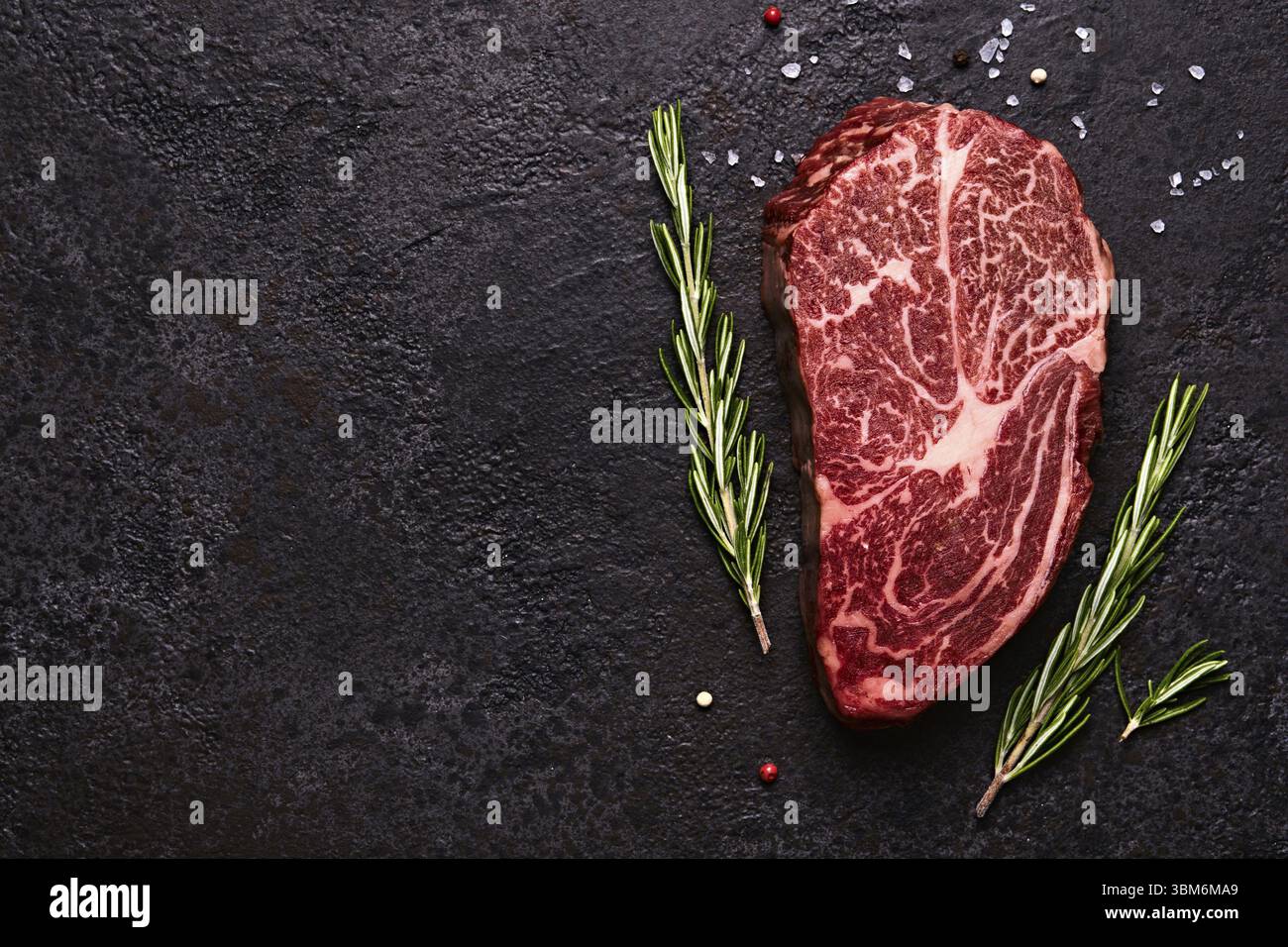 Fresh raw marbled beef rib eye steak and spices on black stone ...