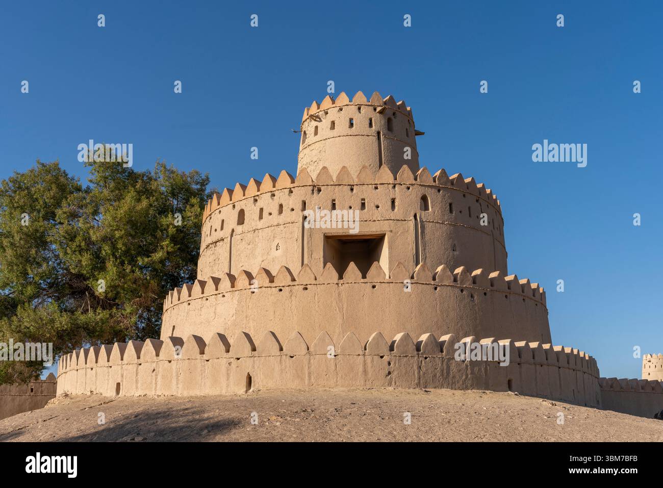 A large circular mud brick tower with stepped crenellations rises above ...