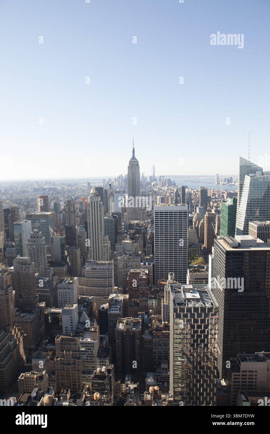 Empire State Building is rising above flat skyline, featuring rooftop towers and river Stock ...