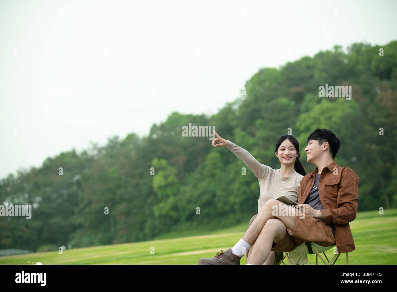 A young Chinese couple sitting on folding chairs sharing content on a ...