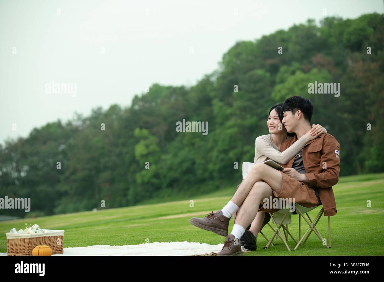 A young Chinese couple sitting on folding chairs sharing content on a ...