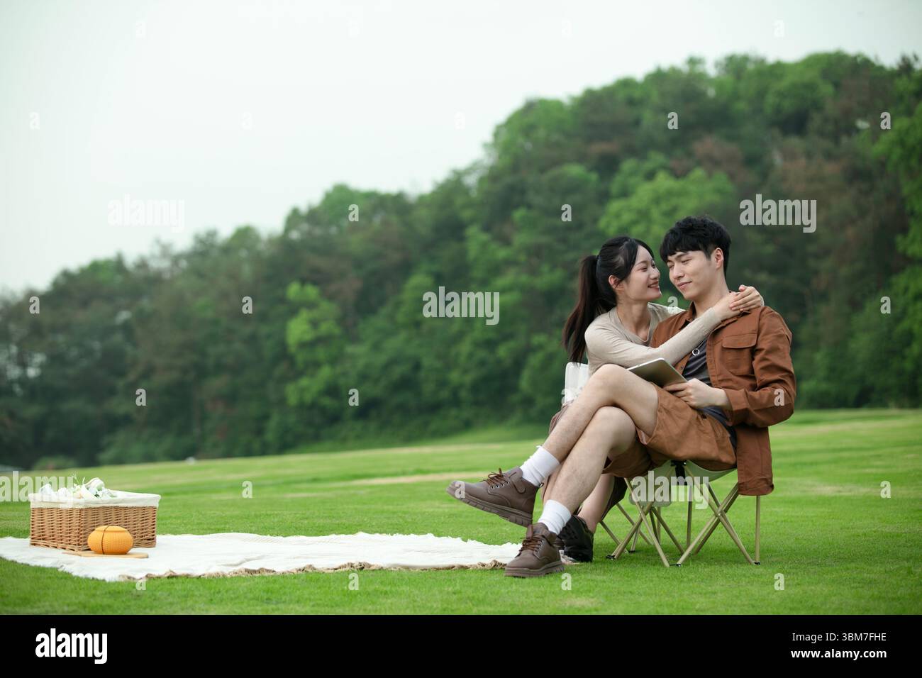 A young Chinese couple sitting on folding chairs sharing content on a ...