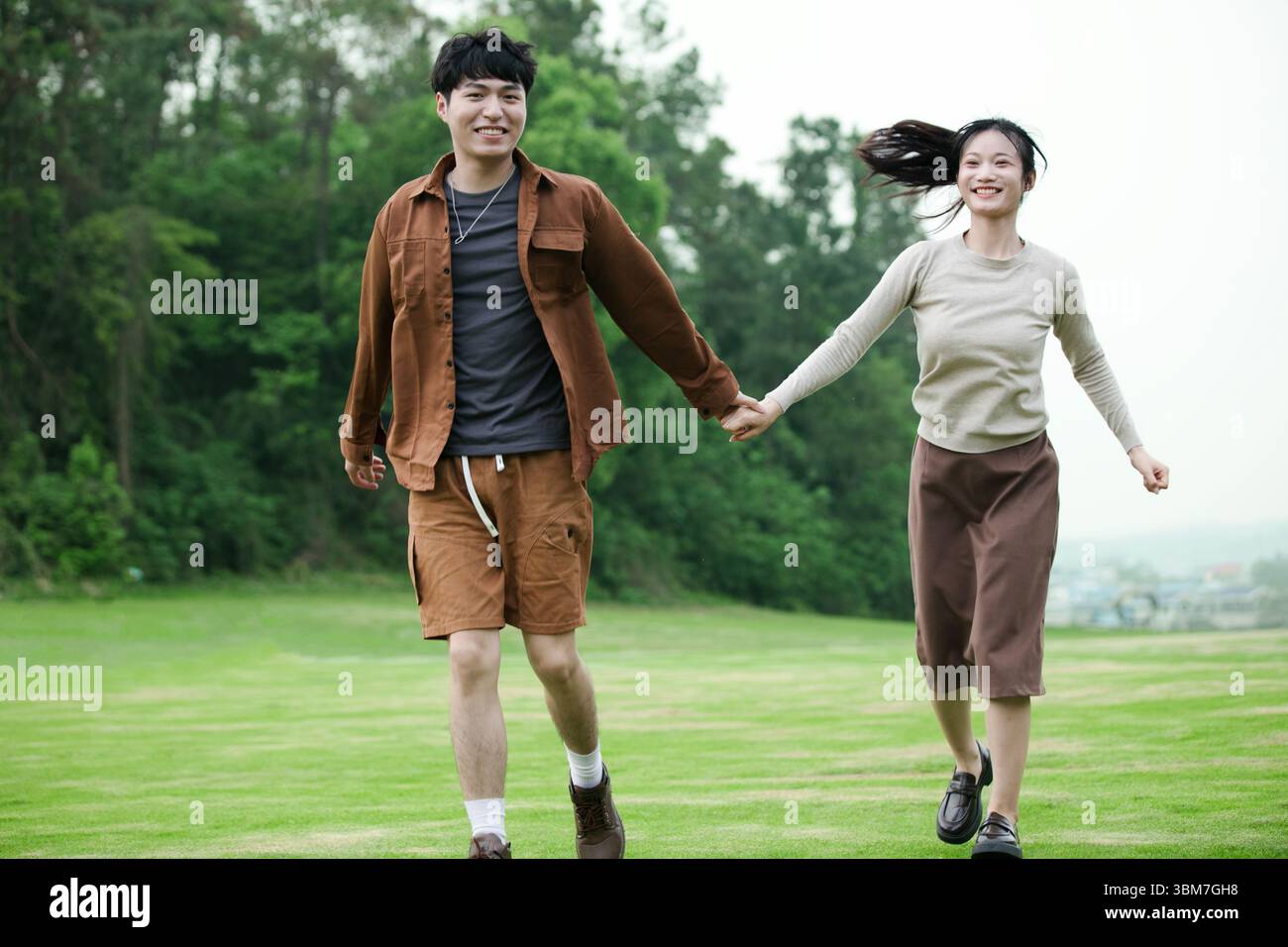 A young couple happily running and chasing each other on the lawn Stock ...
