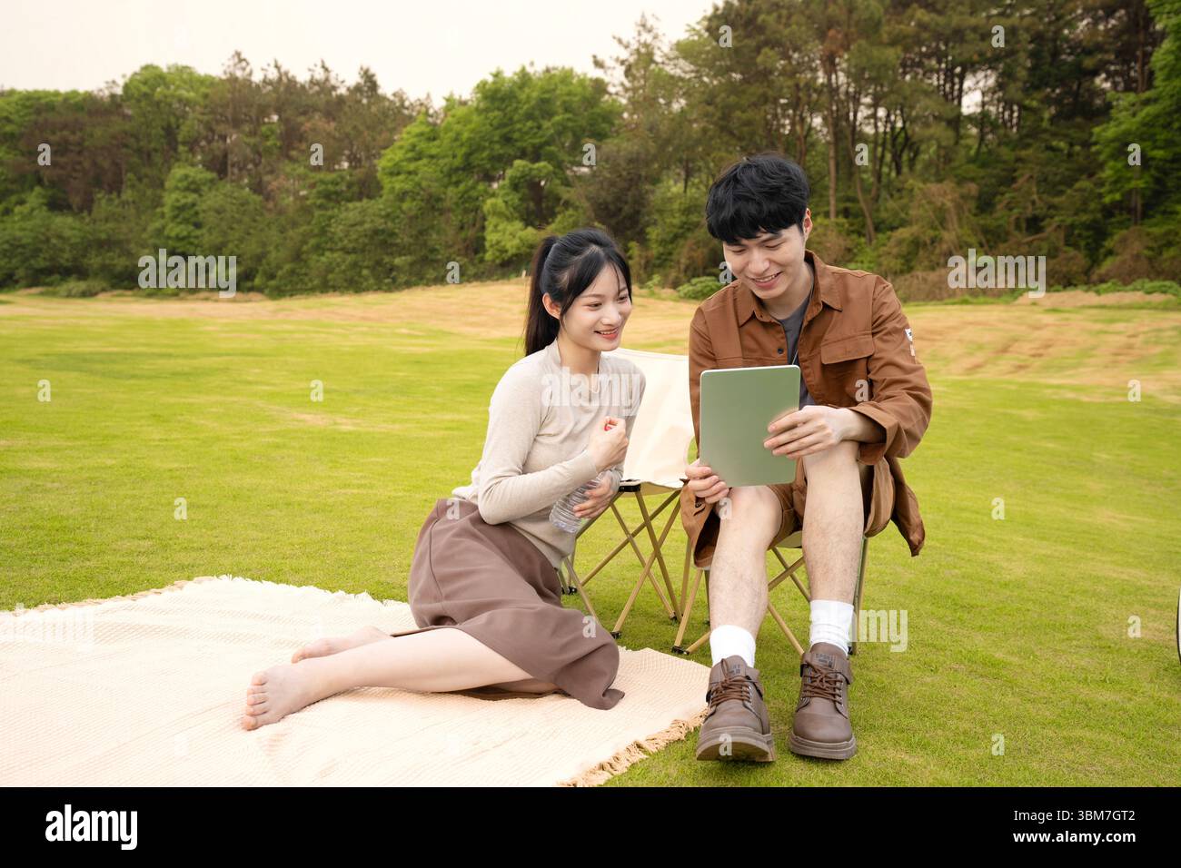 A young Chinese couple sitting on folding chairs sharing content on a ...