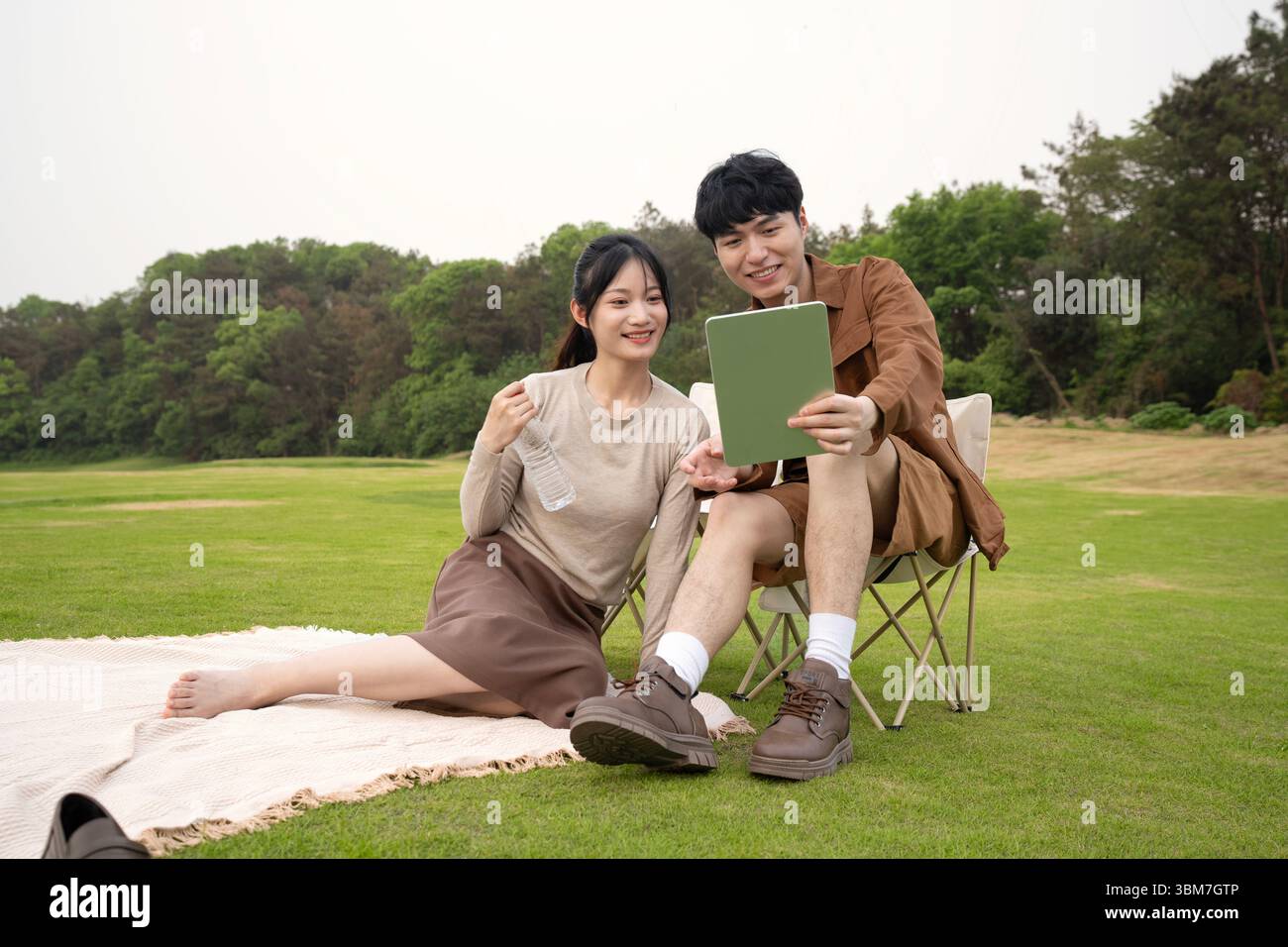 A young Chinese couple sitting on folding chairs sharing content on a ...
