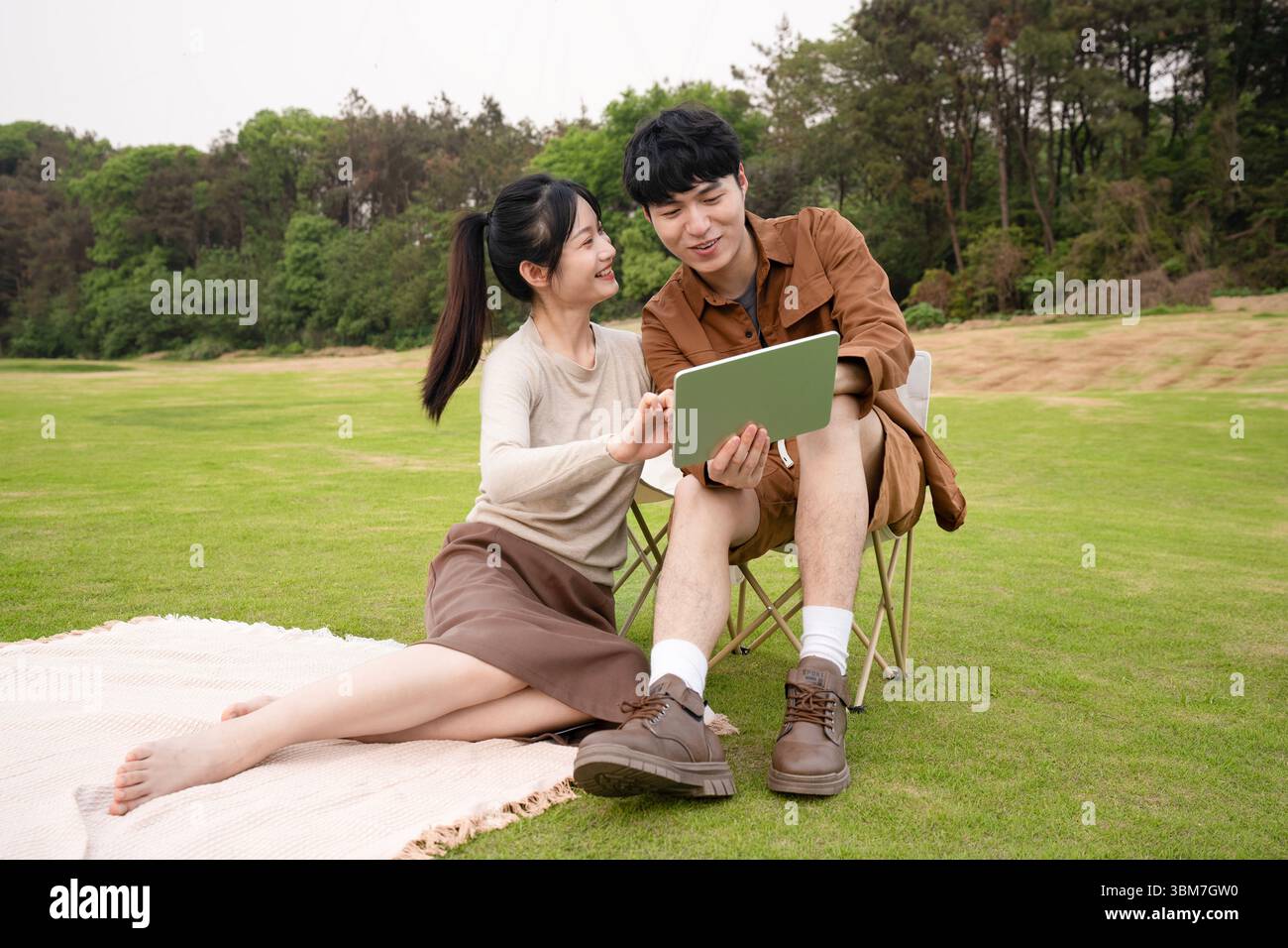 A young Chinese couple sitting on folding chairs sharing content on a ...