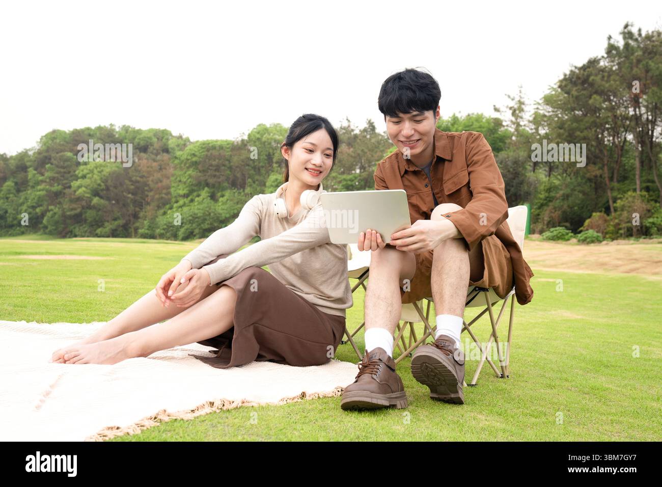 A young Chinese couple sitting on folding chairs sharing content on a ...
