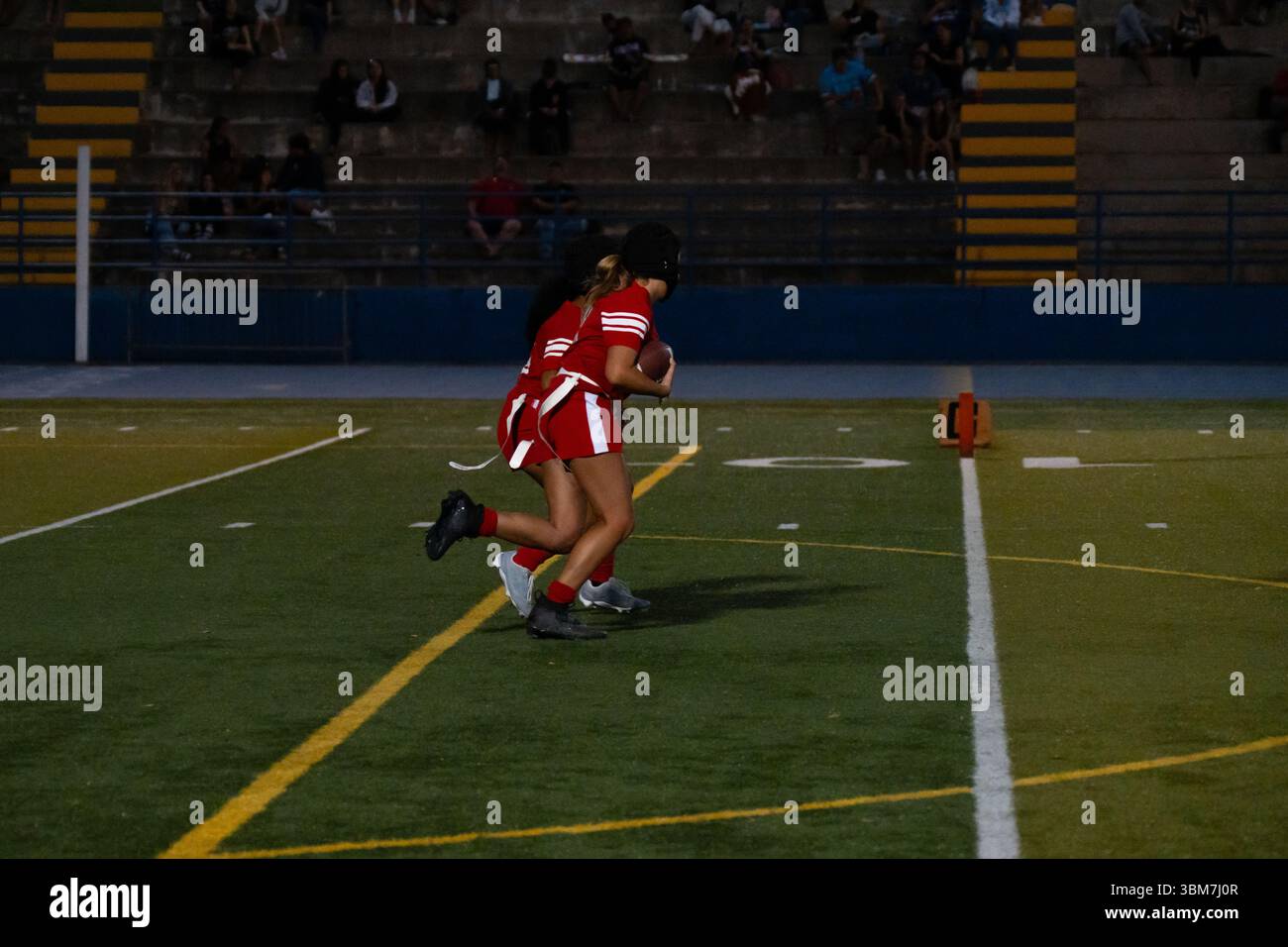 Title: Girls in red uniforms playing flag football on vibrant field ...